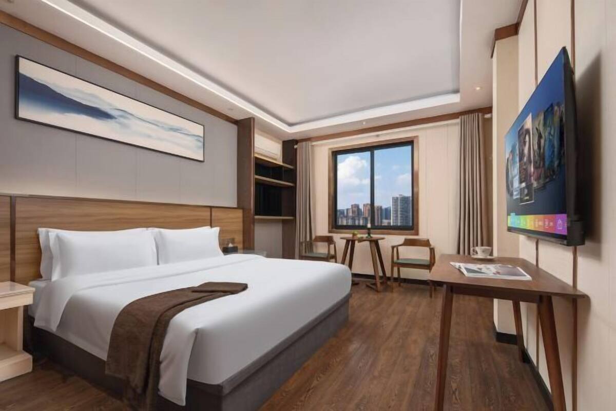 Quarto de hotel com uma cama grande, uma mesa, uma cadeira, uma televisão e uma janela com vista para a cidade.