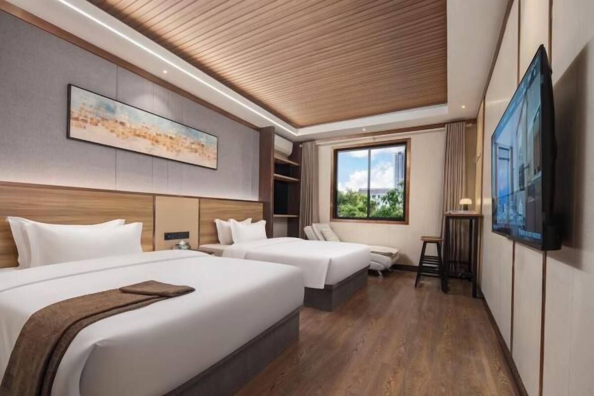 Quarto de hotel com duas camas, uma janela grande, TV de tela plana e um quadro na parede.