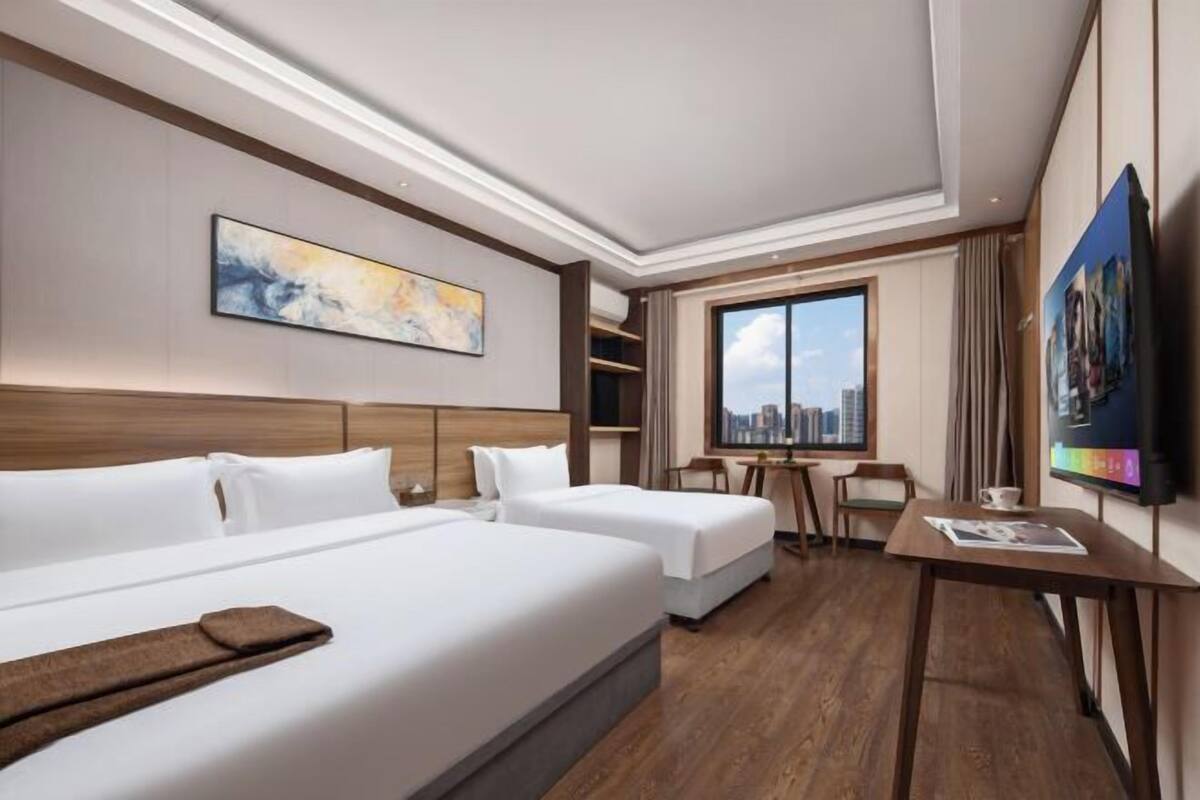 Quarto de hotel com duas camas, vista para a cidade, televisão de tela plana e um quadro na parede.