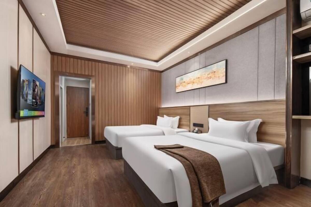 Quarto de hotel com duas camas, painéis de madeira, televisão de tela plana e um quadro na parede.
