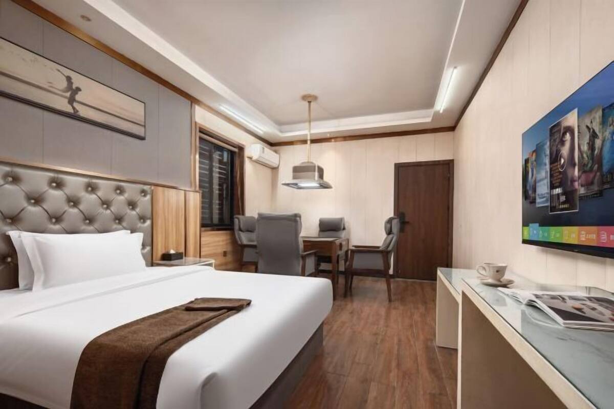 Quarto de hotel com uma cama, escrivaninha, cadeira, televisão e um quadro na parede.