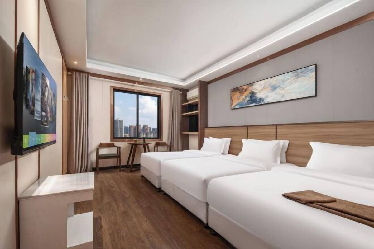 Quarto de hotel com duas camas, uma escrivaninha, uma cadeira, uma televisão e vista para a cidade.