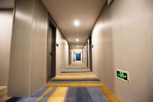 Corredor de hotel com portas em ambos os lados, piso coberto de carpete e placa de saída de emergência na parede.