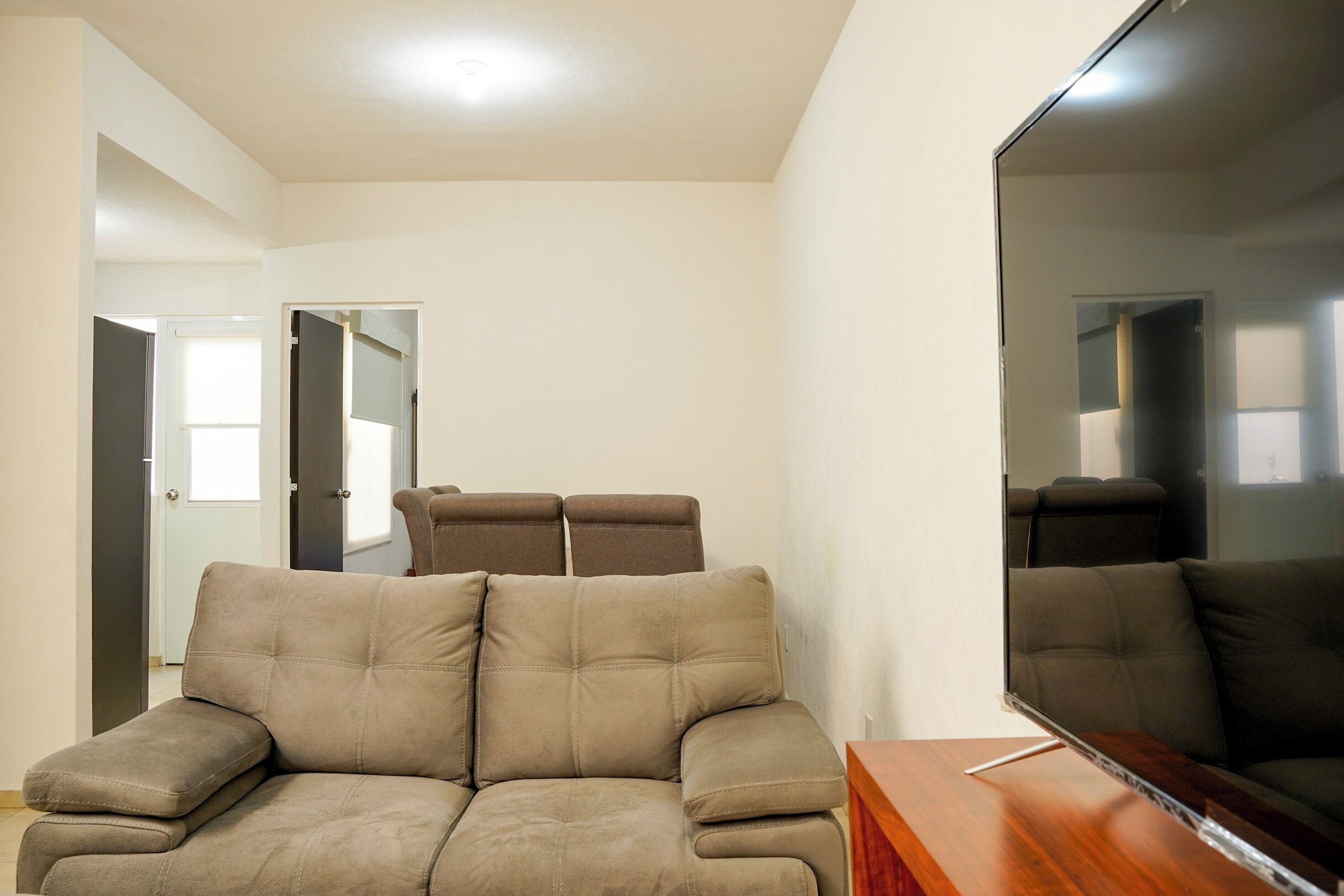 Sala de estar com sofá bege, mesa de centro de madeira e uma televisão de tela grande.