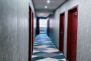 Um corredor com carpete estampado, portas vermelhas e uma parede em tom claro.