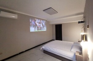 Quarto com cama, tela de projetor e luminária fixada na parede.