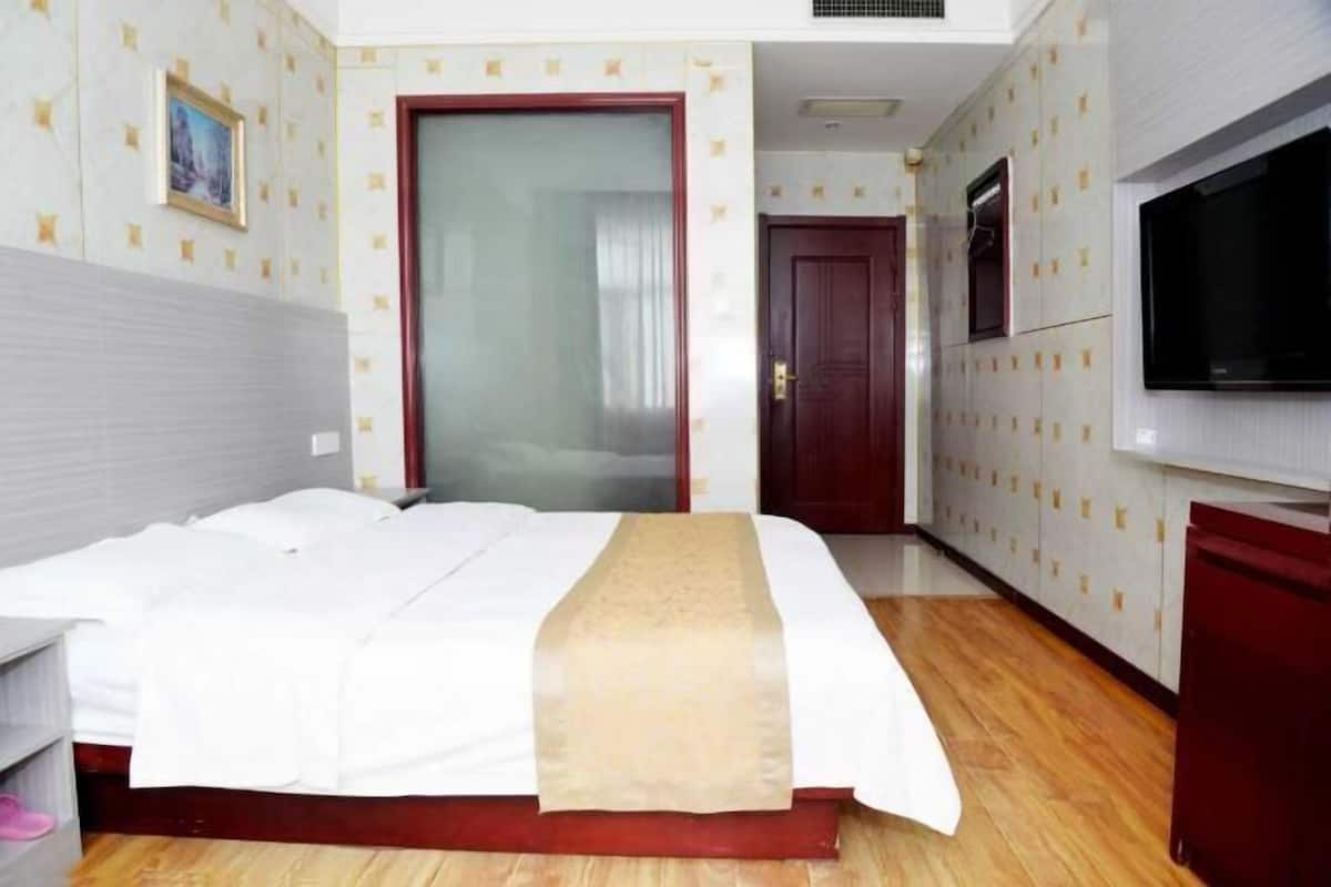 Quarto de hotel com cama, televisão, guarda-roupa e porta que dá para outro espaço.