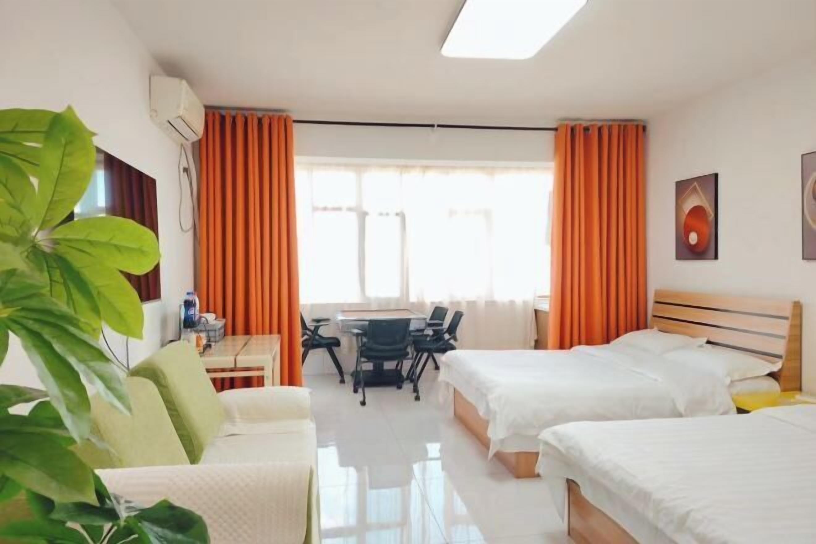 Quarto de hotel com duas camas, uma escrivaninha, cadeiras e uma janela grande com cortinas.