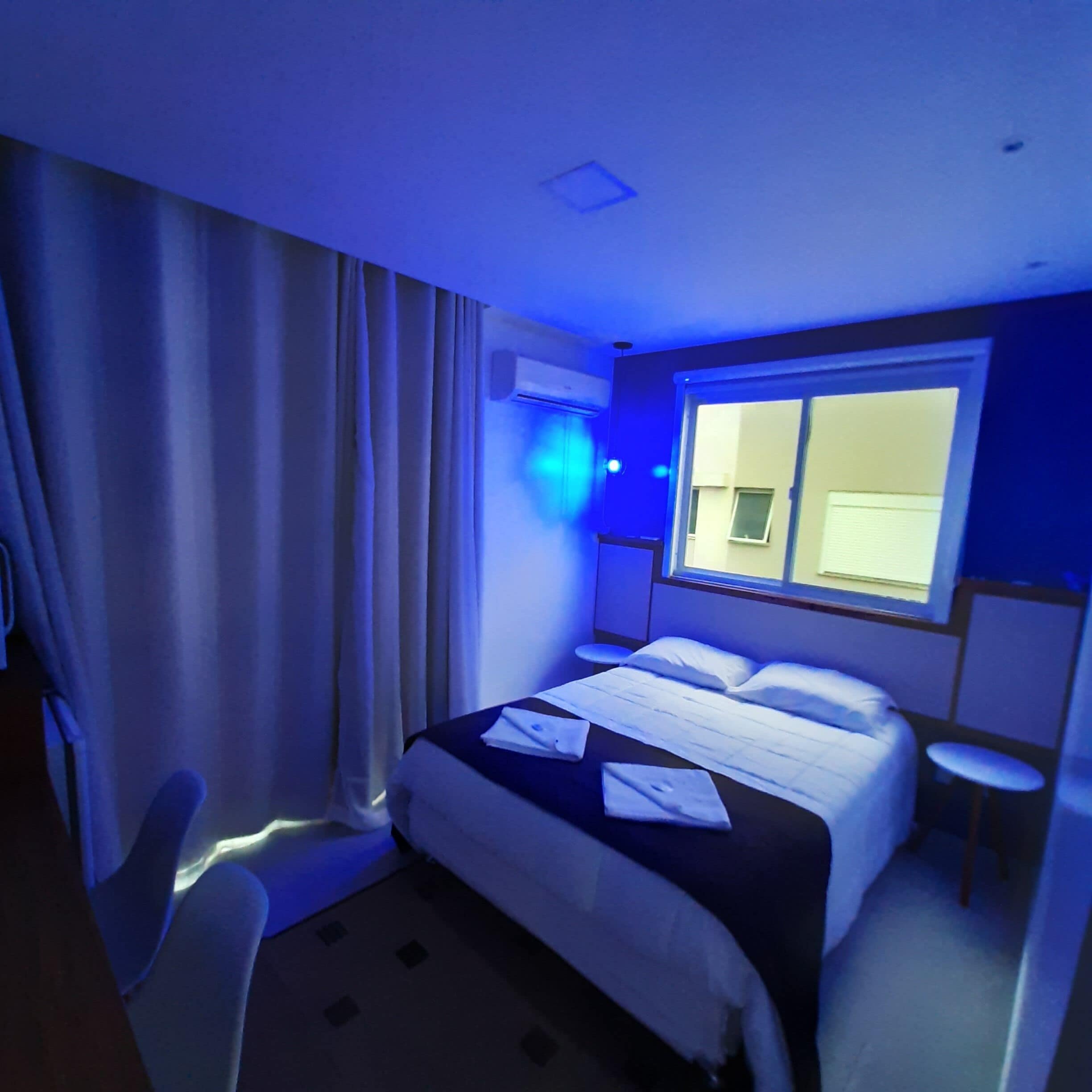 Quarto de hotel com cama, uma cadeira, janela e cortinas.