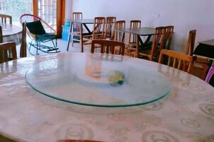 Uma sala de jantar com uma mesa redonda de vidro e cadeiras de madeira ao redor.