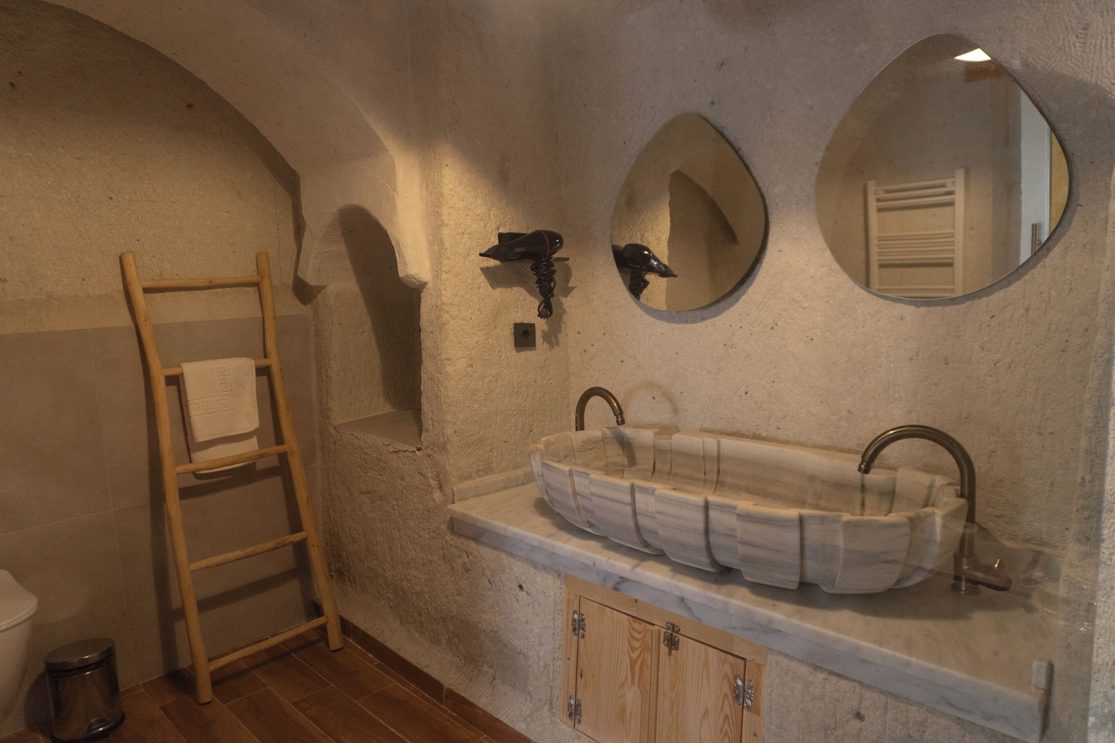 Casa de banho com escada de madeira, lavatório de pedra e três espelhos fixados na parede.