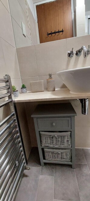 Casa de banho com lavatório, espelho, porta-toalhas e uma pequena estante com produtos de higiene pessoal.