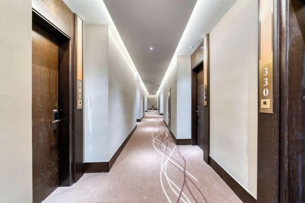 Um corredor de hotel comprido e estreito com portas de ambos os lados, numeradas 301 e 330, e chão coberto de carpete.