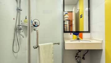 Uma casa de banho com cabine de chuveiro em vidro, lavatório branco com espelho e porta-toalhas.
