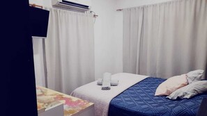 Quarto com uma cama, uma mesinha e uma cortina.