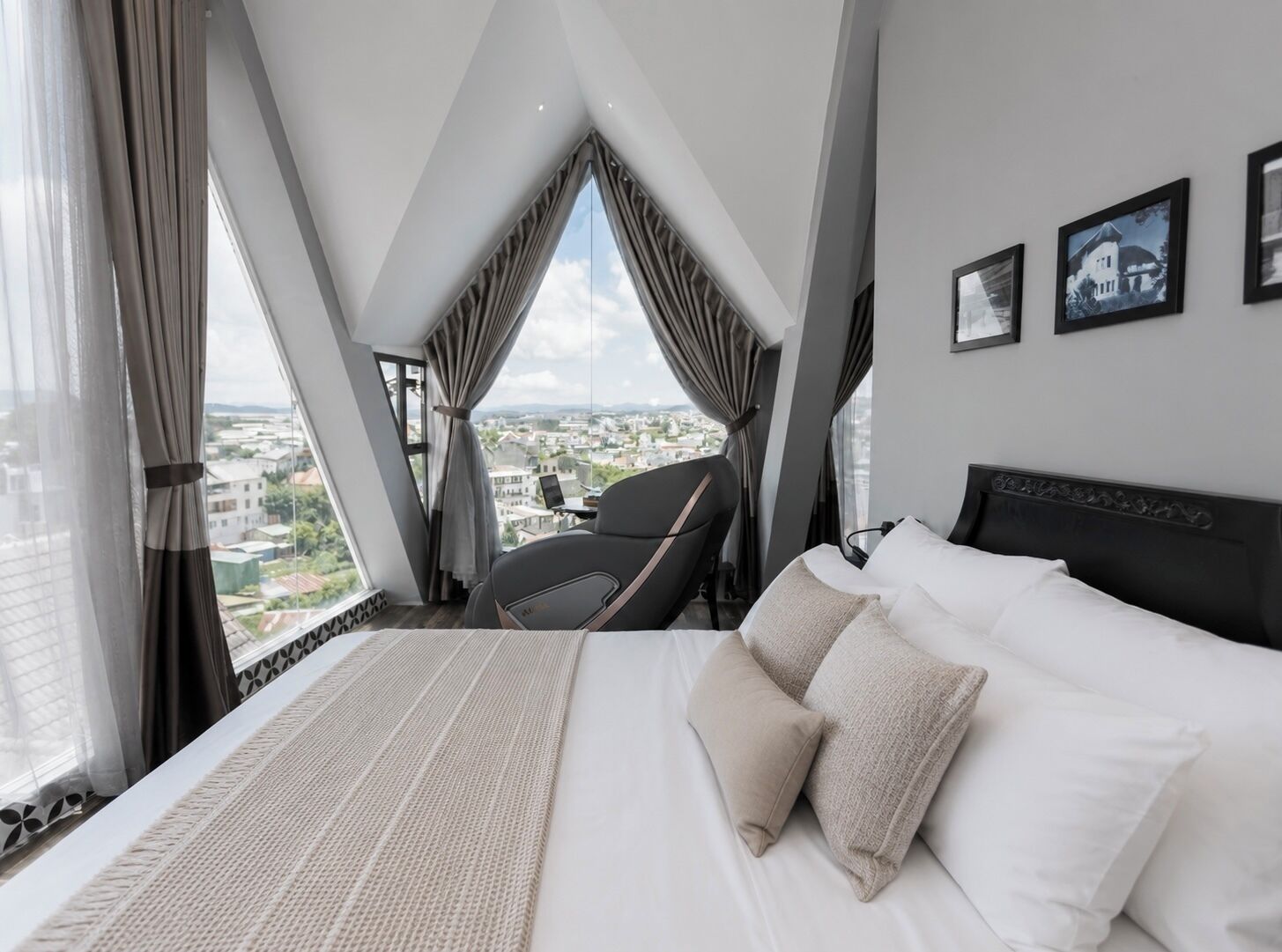 Quarto de hotel moderno com uma cama grande, uma cadeira e vista para a cidade.