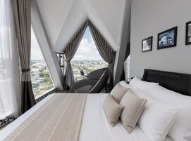 Quarto de hotel moderno com uma cama grande, uma cadeira e vista para a cidade.