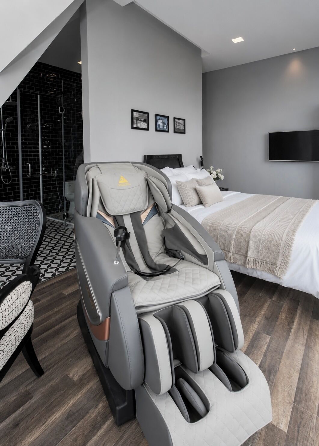 Um quarto moderno com uma poltrona de massagem, uma cama, uma TV e um espaço com chuveiro.