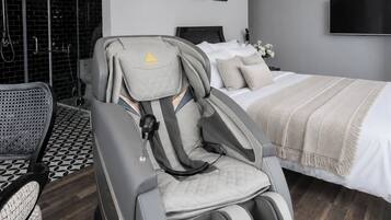 Um quarto moderno com uma poltrona de massagem, uma cama, uma TV e um espaço com chuveiro.