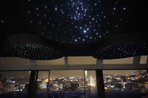 Quarto com teto estrelado e vista da cidade através de grandes janelas.