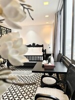 Quarto de hotel com uma cama, uma mesa com chaleira, uma cadeira e vista para o exterior através de amplas janelas.