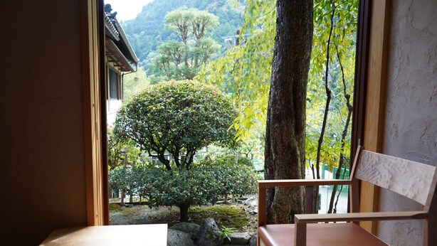 Quarto com um banco de madeira e vista para um jardim com uma árvore grande e pedras.
