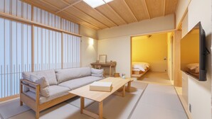 Um quarto em estilo japonês tradicional, com tatames, uma mesa de madeira baixa, um sofá e uma televisão fixada na parede.