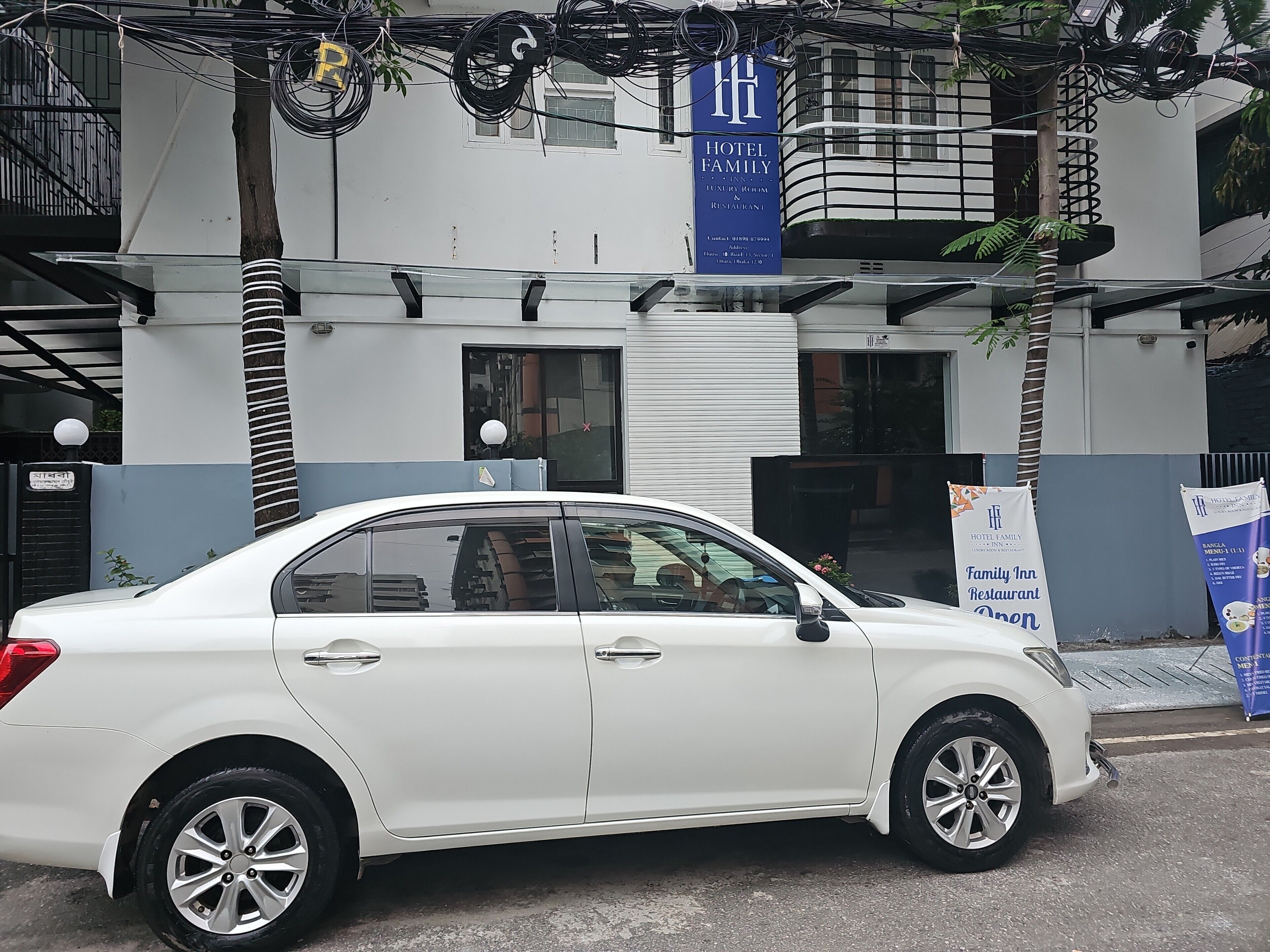 Um carro branco estacionado em frente a um prédio com uma placa que diz 'HOTEL FAMILY'.