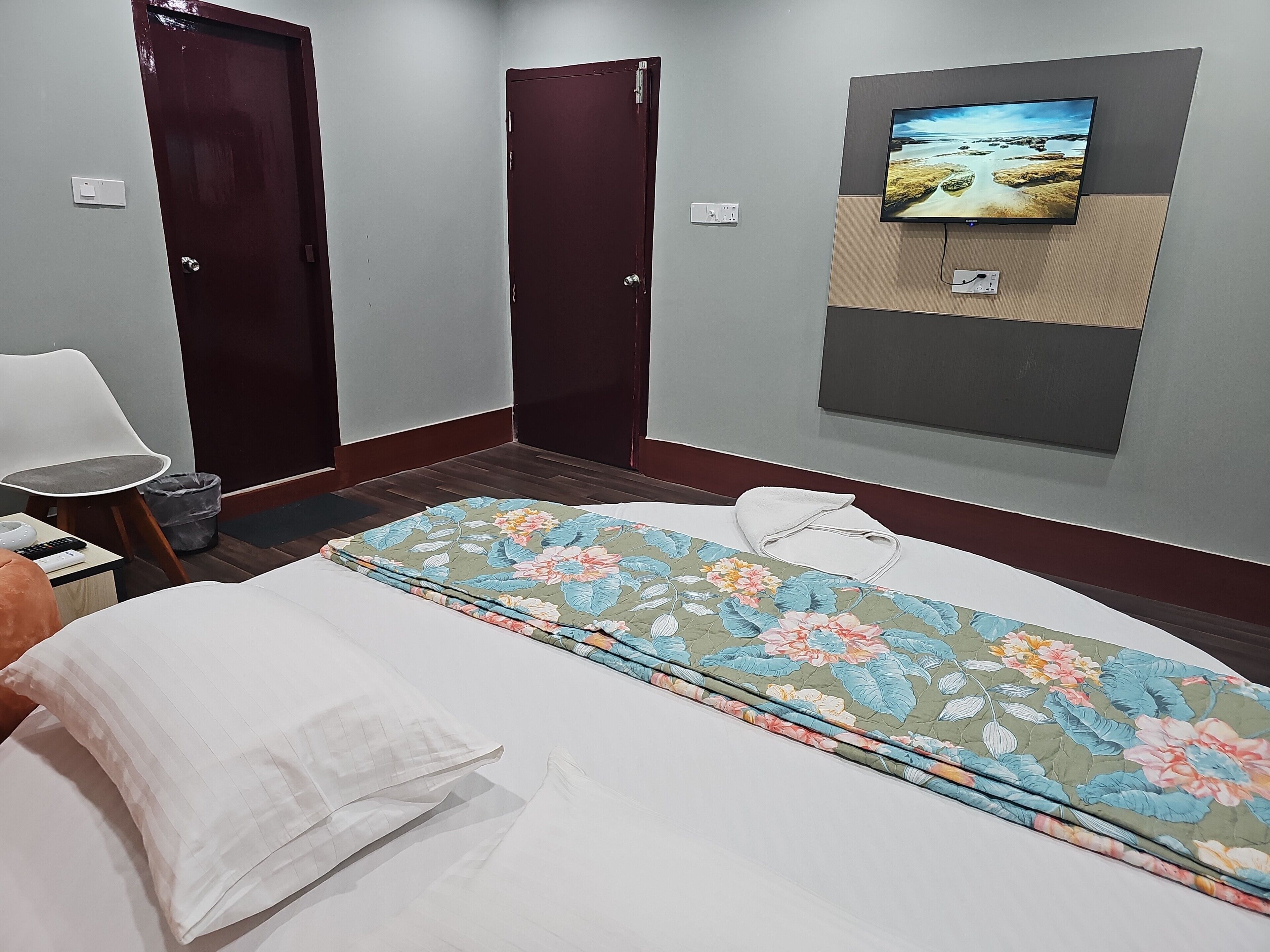 Quarto de hotel com cama, televisão na parede, cadeira e secretária com controle remoto.