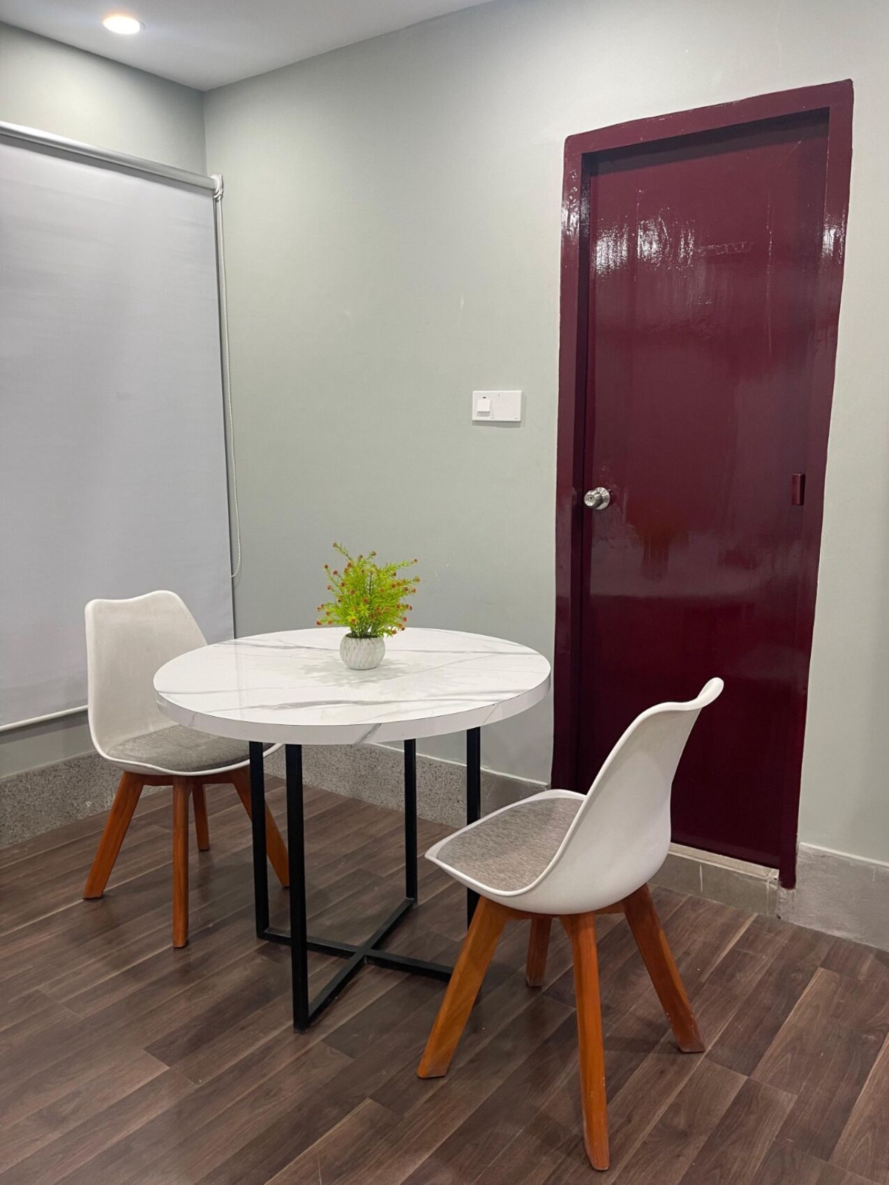 Uma sala de conferências com uma mesa redonda, duas cadeiras, uma planta em vaso e uma porta vermelha.