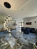 Um lobby moderno com piso de mármore, balcão de recepção e área de estar com sofás.