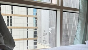 Quarto de hotel com uma janela grande, uma cama e vista para um edifício.