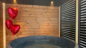 Uma banheira de hidromassagem em uma cabana de madeira, com parede de madeira e janela com persianas horizontais.