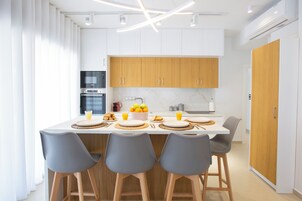 Uma cozinha moderna com armários brancos, uma ilha central com banquetas e um forno embutido.