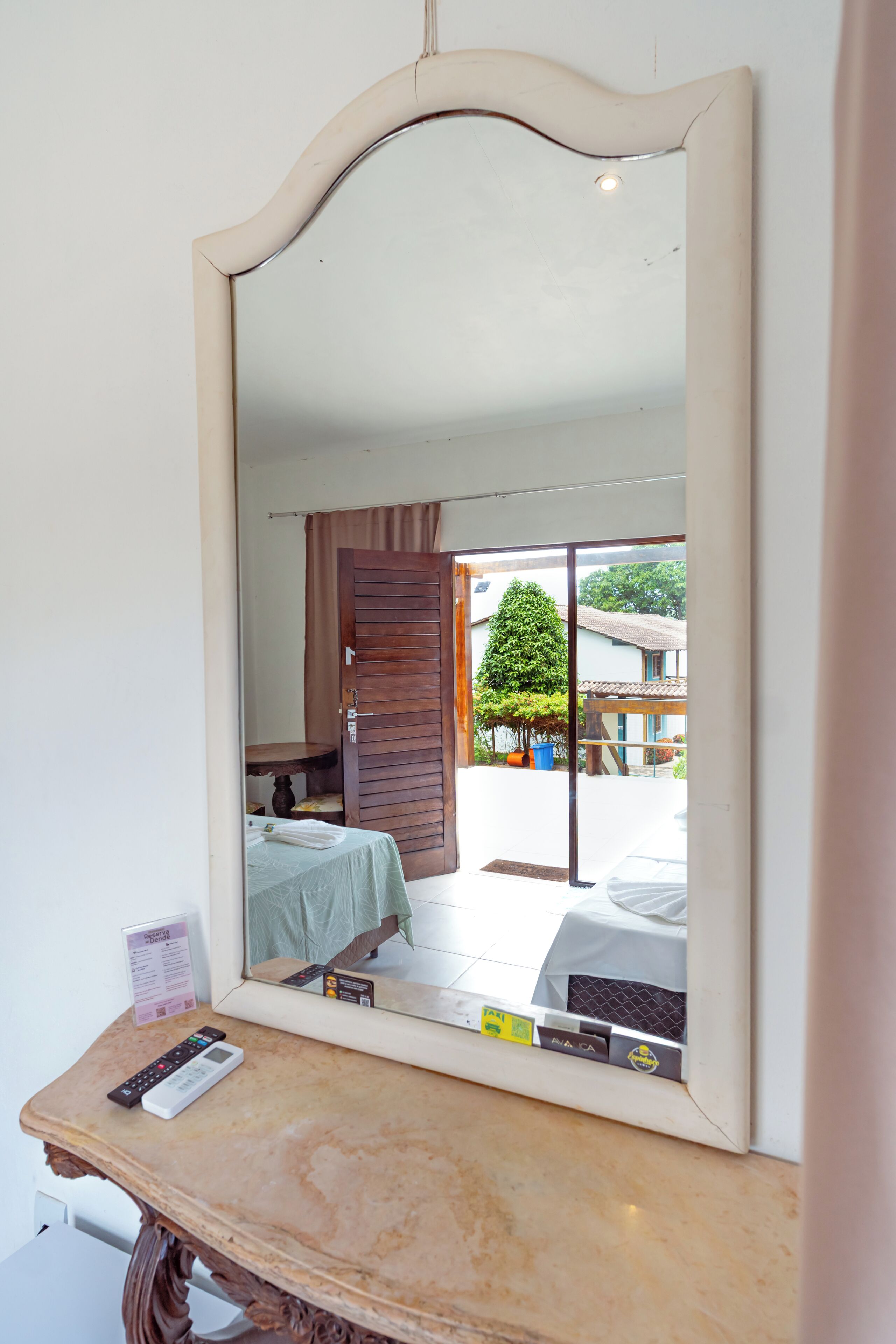 Quarto com um espelho grande, uma cama, uma mesa de cabeceira com um controle remoto e vista para o exterior.