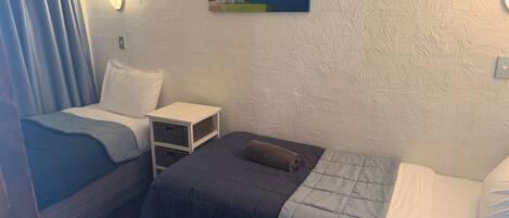 Um quarto com duas camas, uma mesa de cabeceira, um quadro de um farol e uma janela com cortinas.