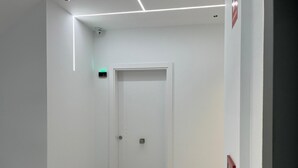 Um corredor com uma porta branca, uma câmera de segurança e uma placa de saída verde.