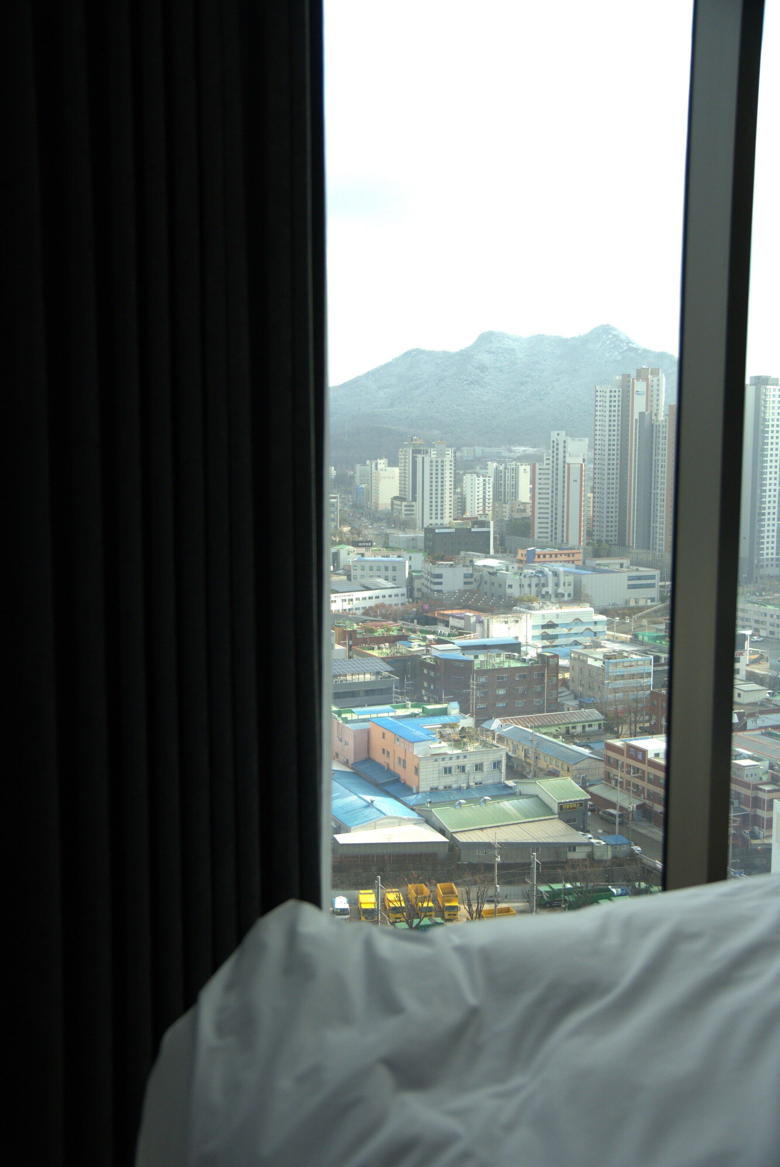 Quarto de hotel com uma grande janela que oferece vista para a paisagem urbana e montanhas.