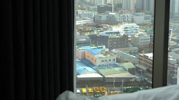 Quarto de hotel com uma grande janela que oferece vista para a paisagem urbana e montanhas.