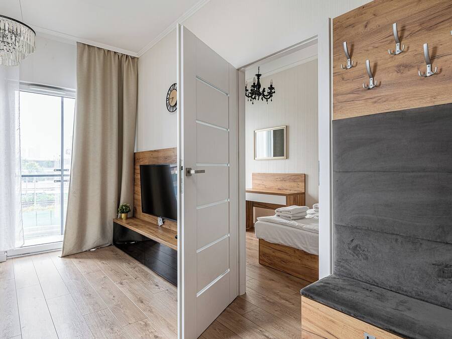 Quarto moderno com uma cama grande, televisão, cabeceira de madeira, mesa de cabeceira e janela com cortinas.