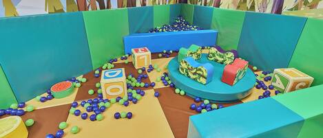 Uma área de recreação colorida, com piscina de bolinhas, estruturas de jogos e uma decoração de melancia.