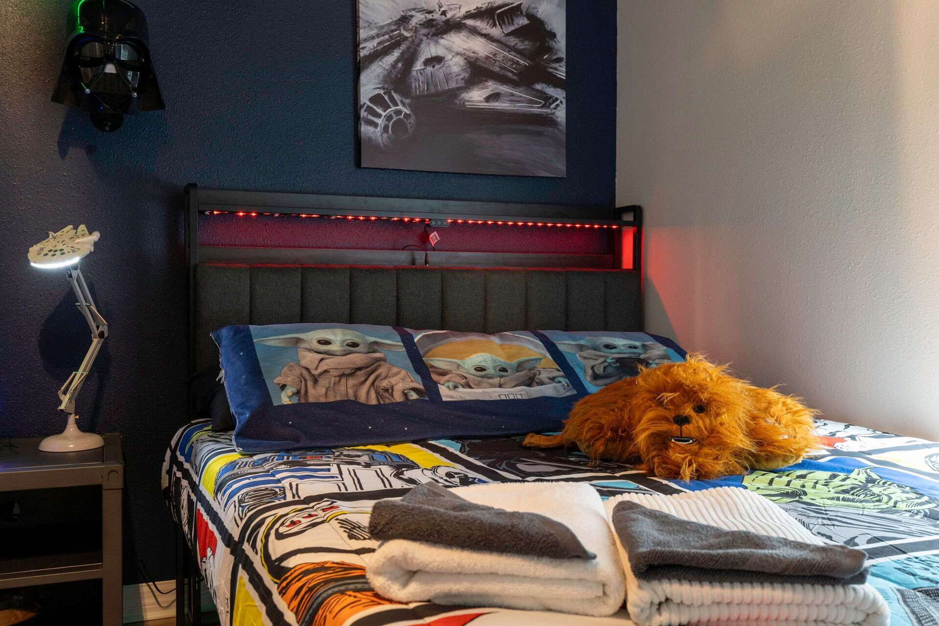 Quarto com colcha temática de Star Wars, um capacete de Darth Vader e um pôster de Star Wars na parede.