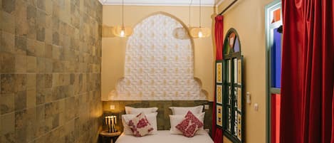 Quarto de hotel com uma cama, um painel decorativo, uma janela com cortinas e um lustre.