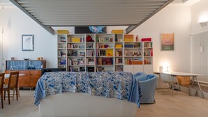 Uma sala de estar moderna com um sofá, uma estante, um espaço de refeições e uma mesa pequena.