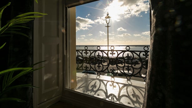 Vista da janela com varanda, um lampião de rua e céu claro com nuvens.
