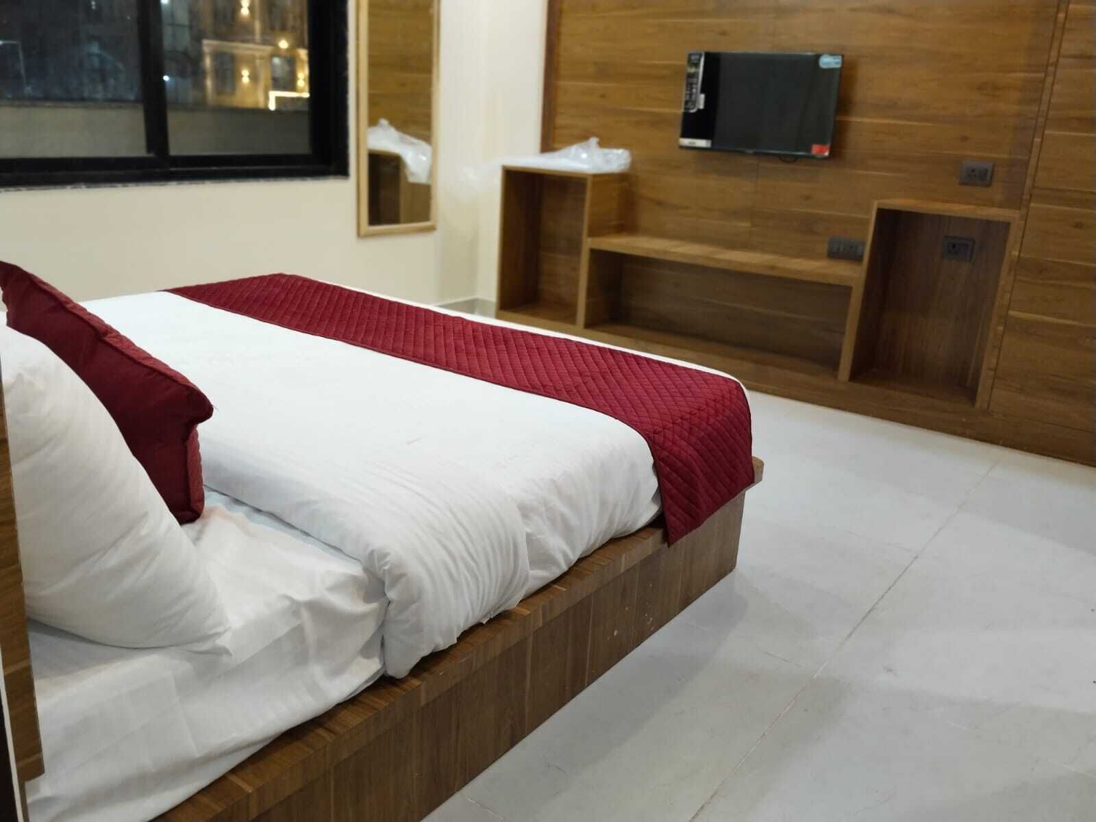 Quarto moderno com estrutura de cama de madeira, roupa de cama branca e manta vermelha.