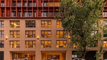 Um hotel com várias andares, fachada moderna, grandes janelas e uma árvore em primeiro plano.