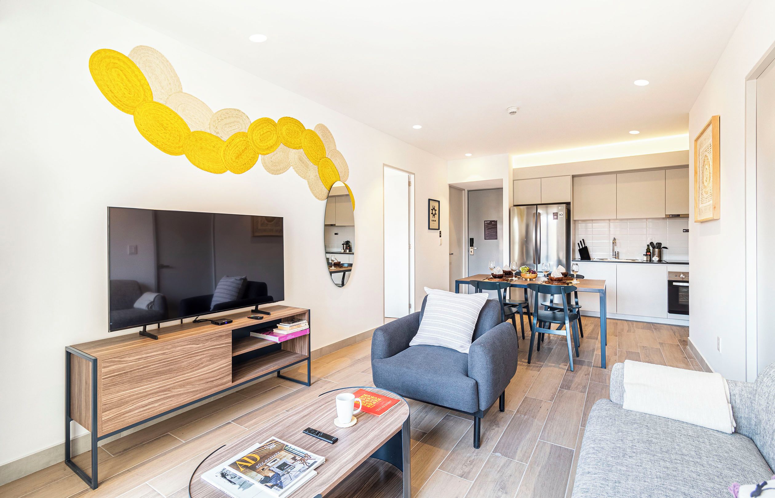 Uma sala de estar moderna com televisão de tela plana, uma mesa de centro com revistas, um sofá e um espaço de jantar com mesa e cadeiras.