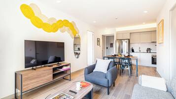 Uma sala de estar moderna com televisão de tela plana, uma mesa de centro com revistas, um sofá e um espaço de jantar com mesa e cadeiras.
