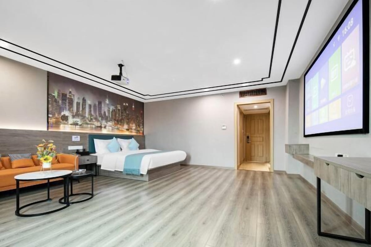 Quarto de hotel moderno com cama, sofá, escrivaninha e uma tela grande.